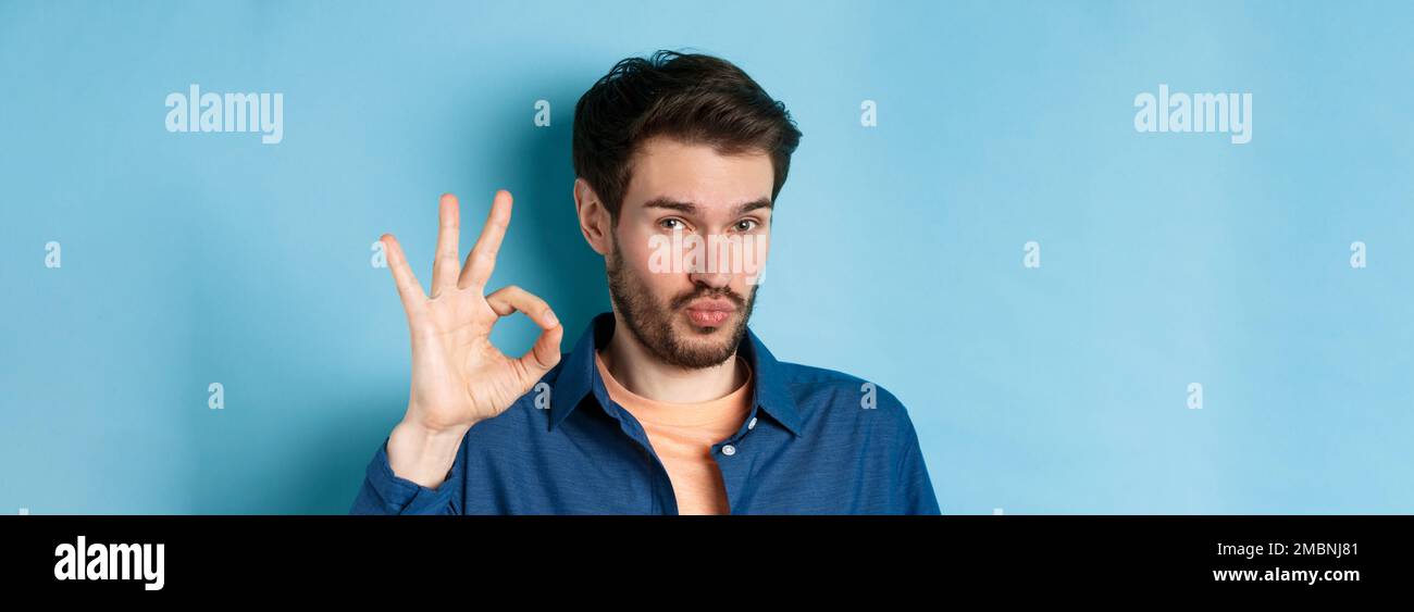 Image of silly young man pucker lips and show okay gesture, praise good ...