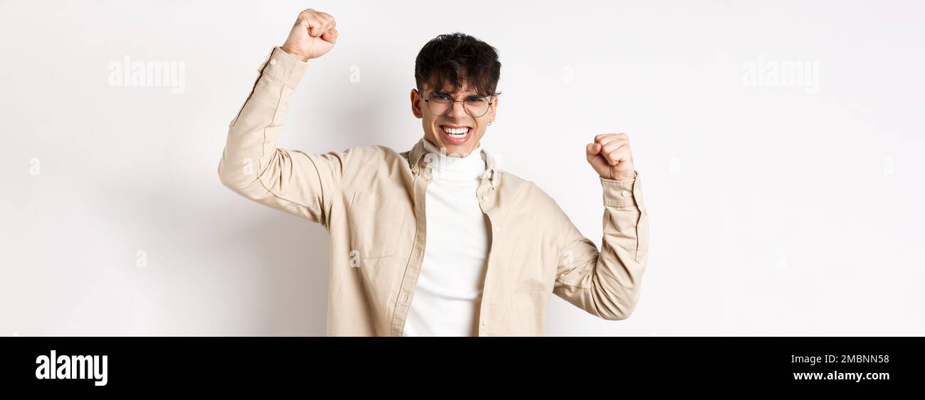 Portrait of motivated young man feeling joy, raising hands up and ...