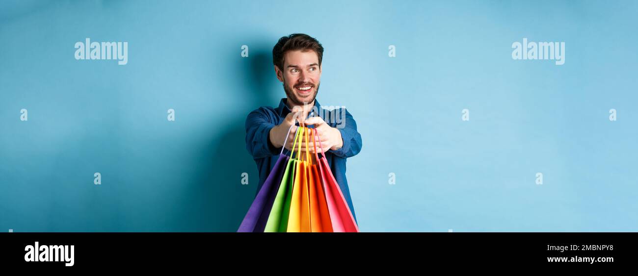 Handsome happy guy smiling, stretch out hands with shopping bags and ...