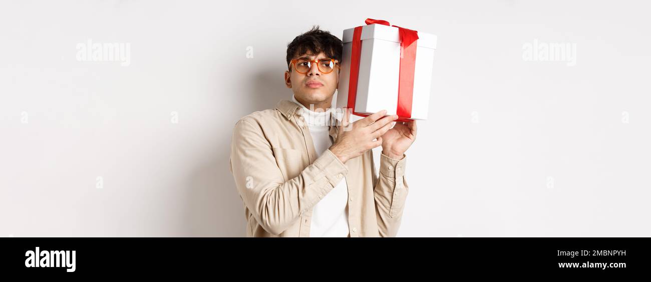 Intrigued guy listening whats inside gift box, trying guess present ...