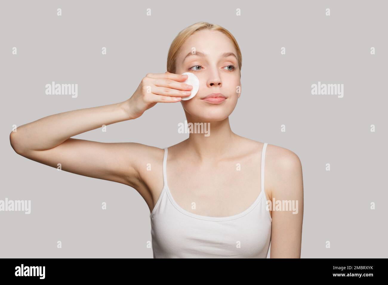 Perfect young blonde woman removing makeup from her face using cotton ...