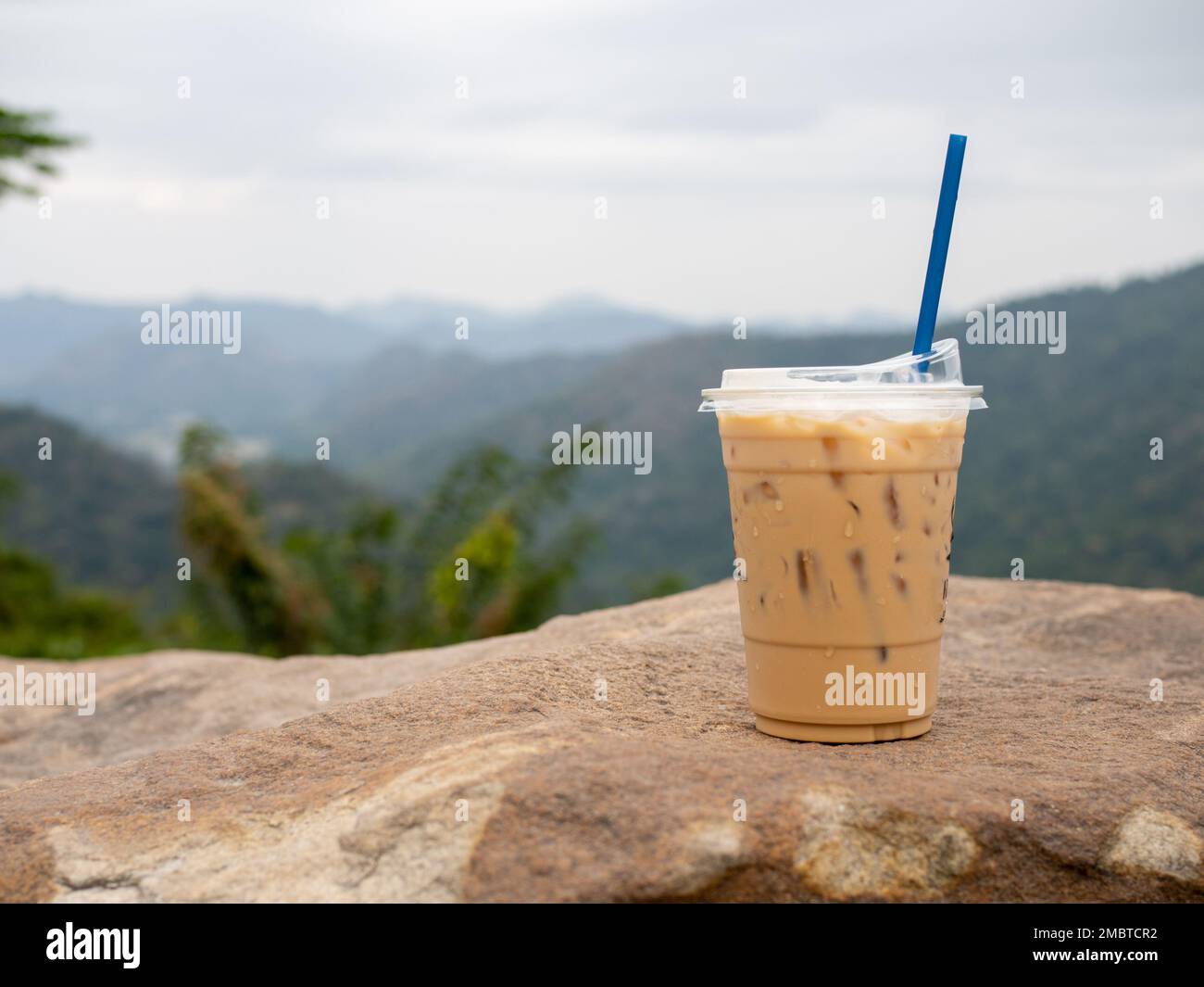 A glass of iced coffee is placed on a rock against a background of ...