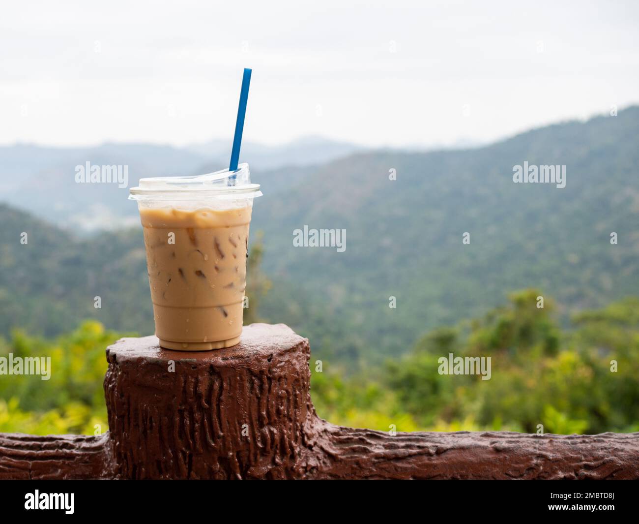 A glass of iced coffee is placed on the fence against a backdrop of ...