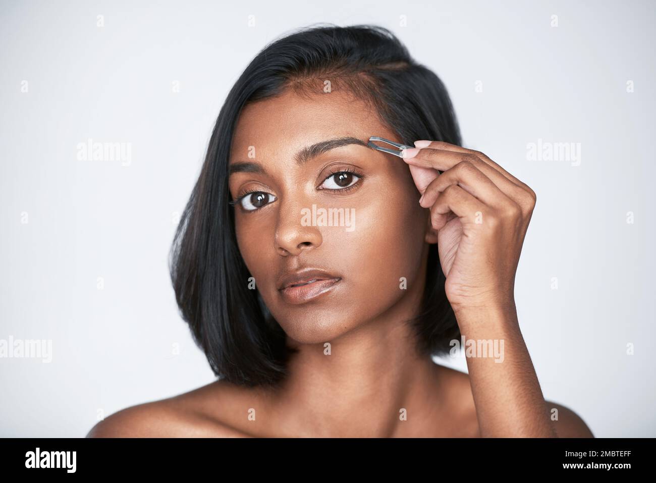 Rough around the edges. a beautiful young woman tweezing her eyebrows ...