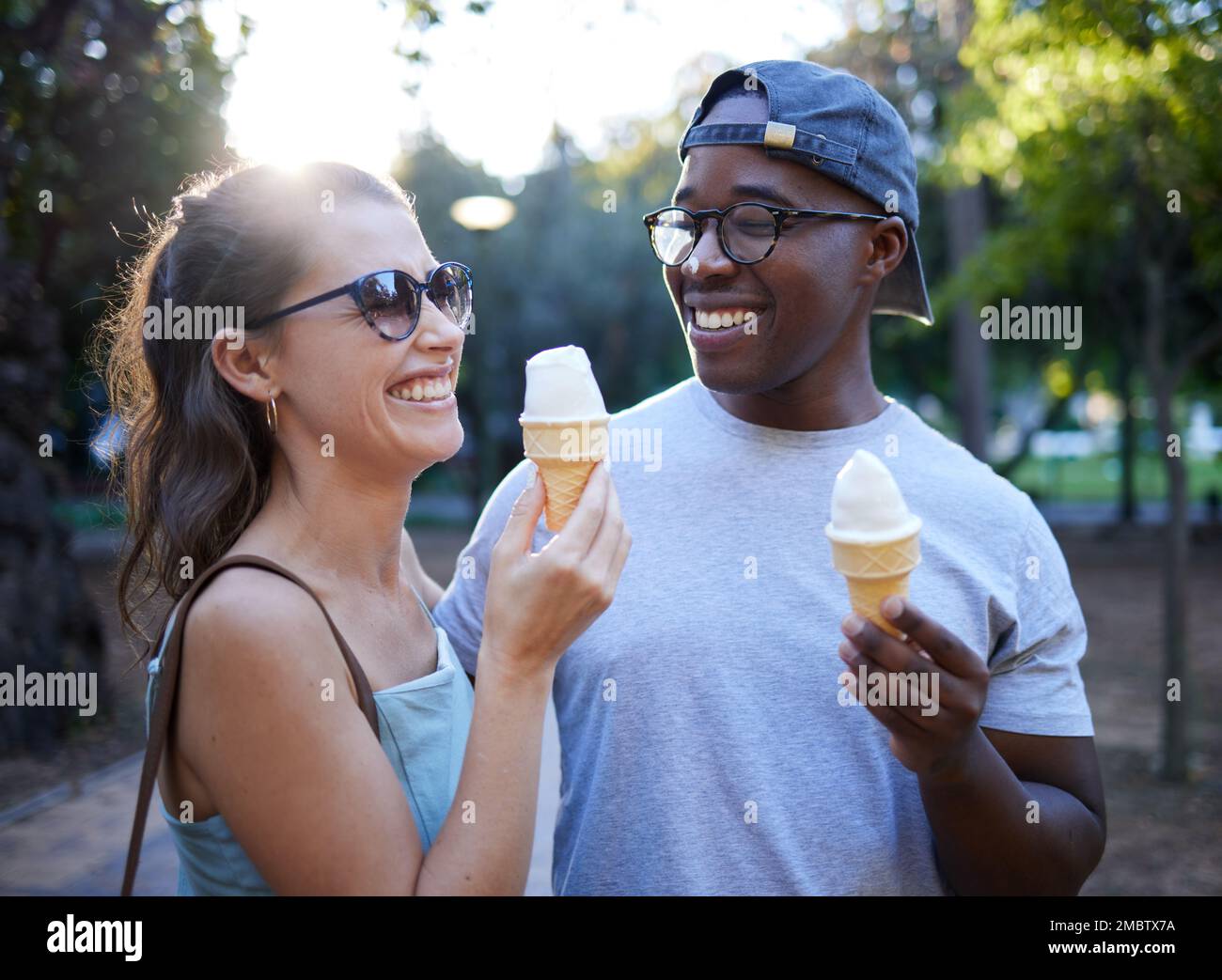 Interracial couple, laughing and ice cream in a park for funny joke ...