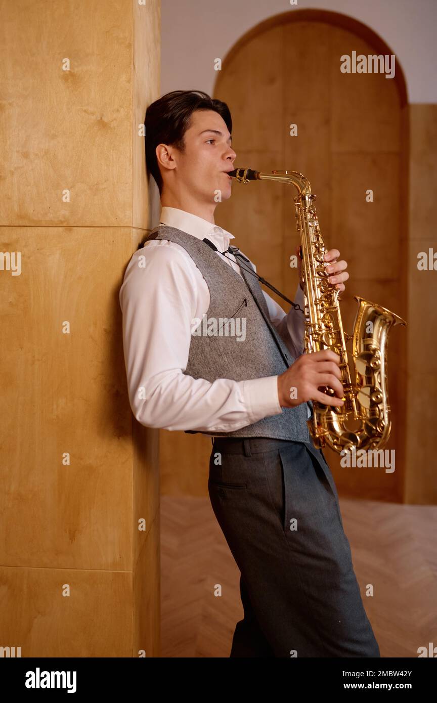Jazz musician playing saxophone and leaning against art studio wall ...