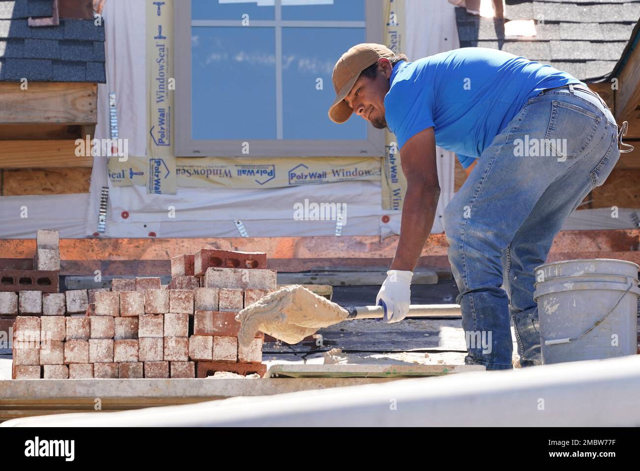 A mason shovels a cement mixture as he prepares to lay down bricks on ...
