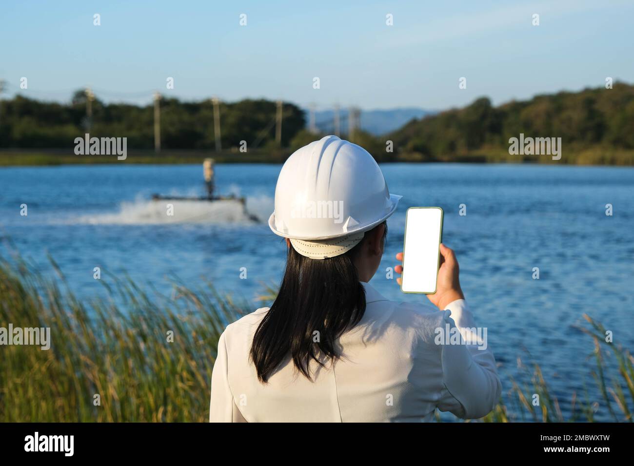 Environmental engineer wearing a white helmet uses a mobile phone to ...