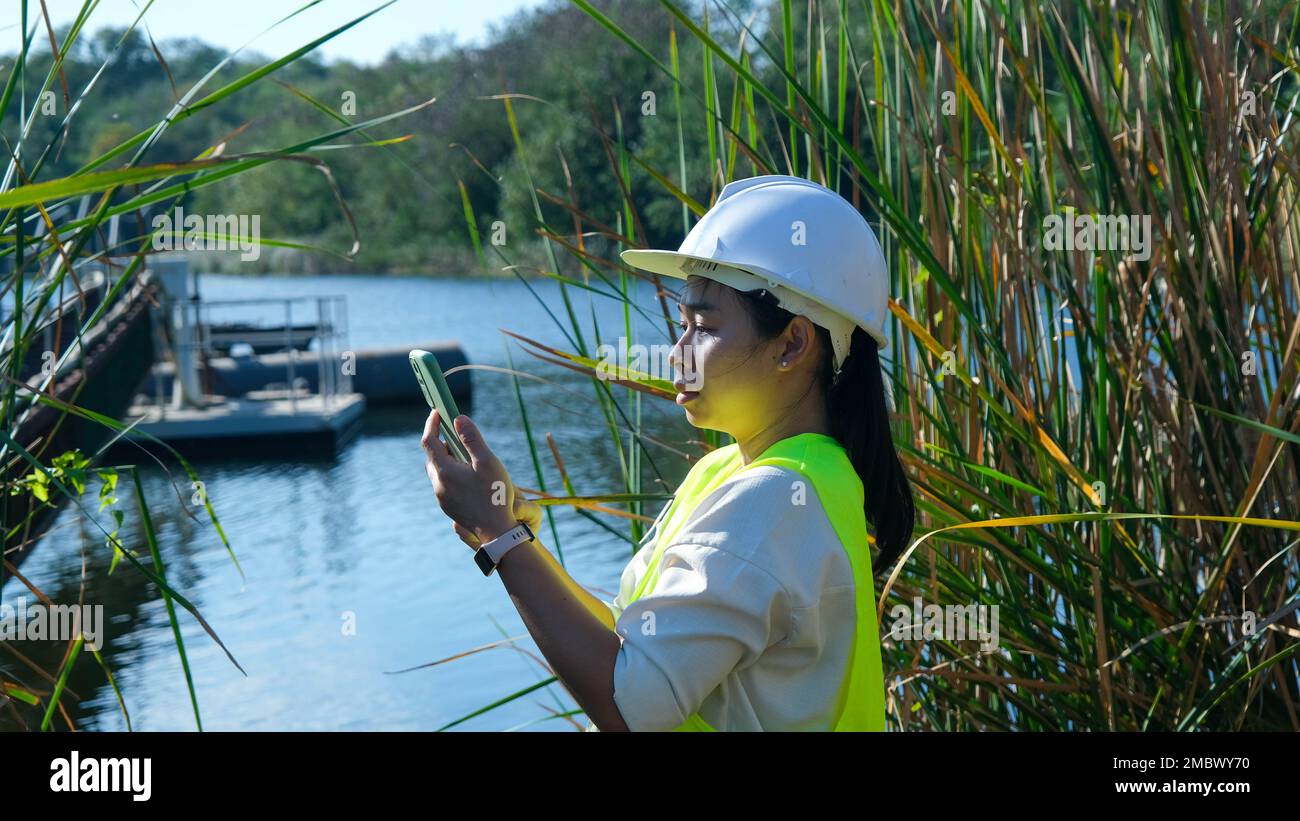 Environmental engineer wearing a white helmet uses a mobile phone to ...