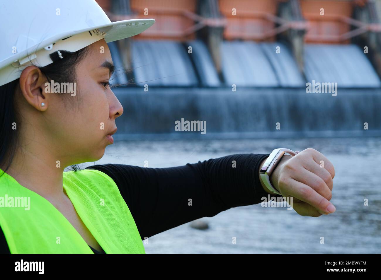 Female engineer in white hat looking at smartwatch while working ...