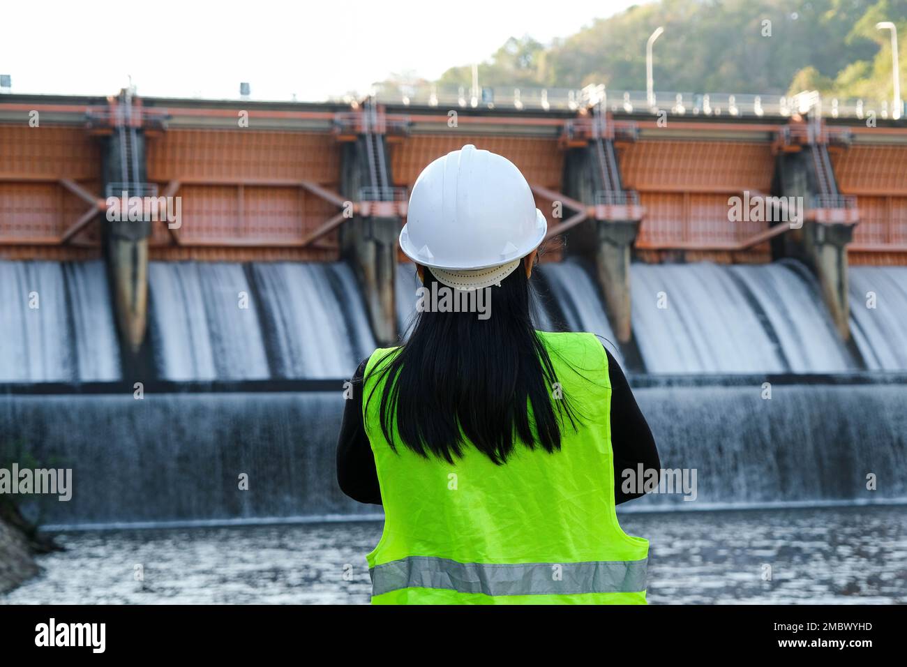 Rear view of female engineer in green vest and helmet standing outside ...