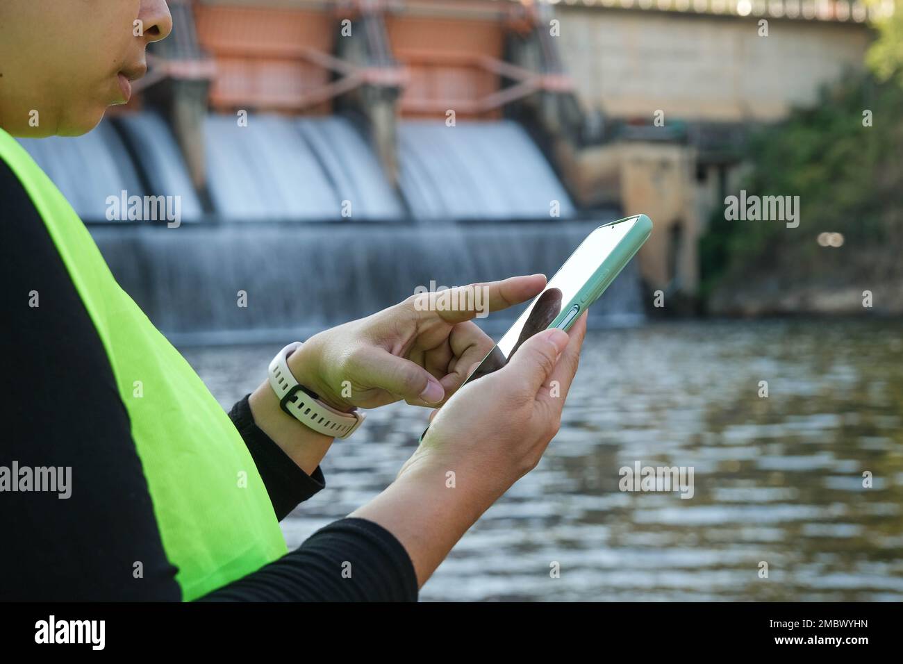 Female engineer in white hat working with smartphone and looking away ...