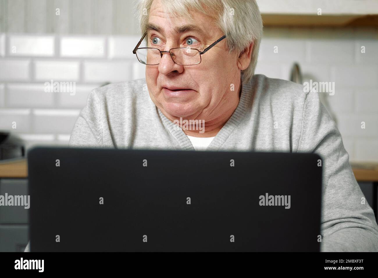 Senior grey haired man wearing glasses sitting at laptop and making ...