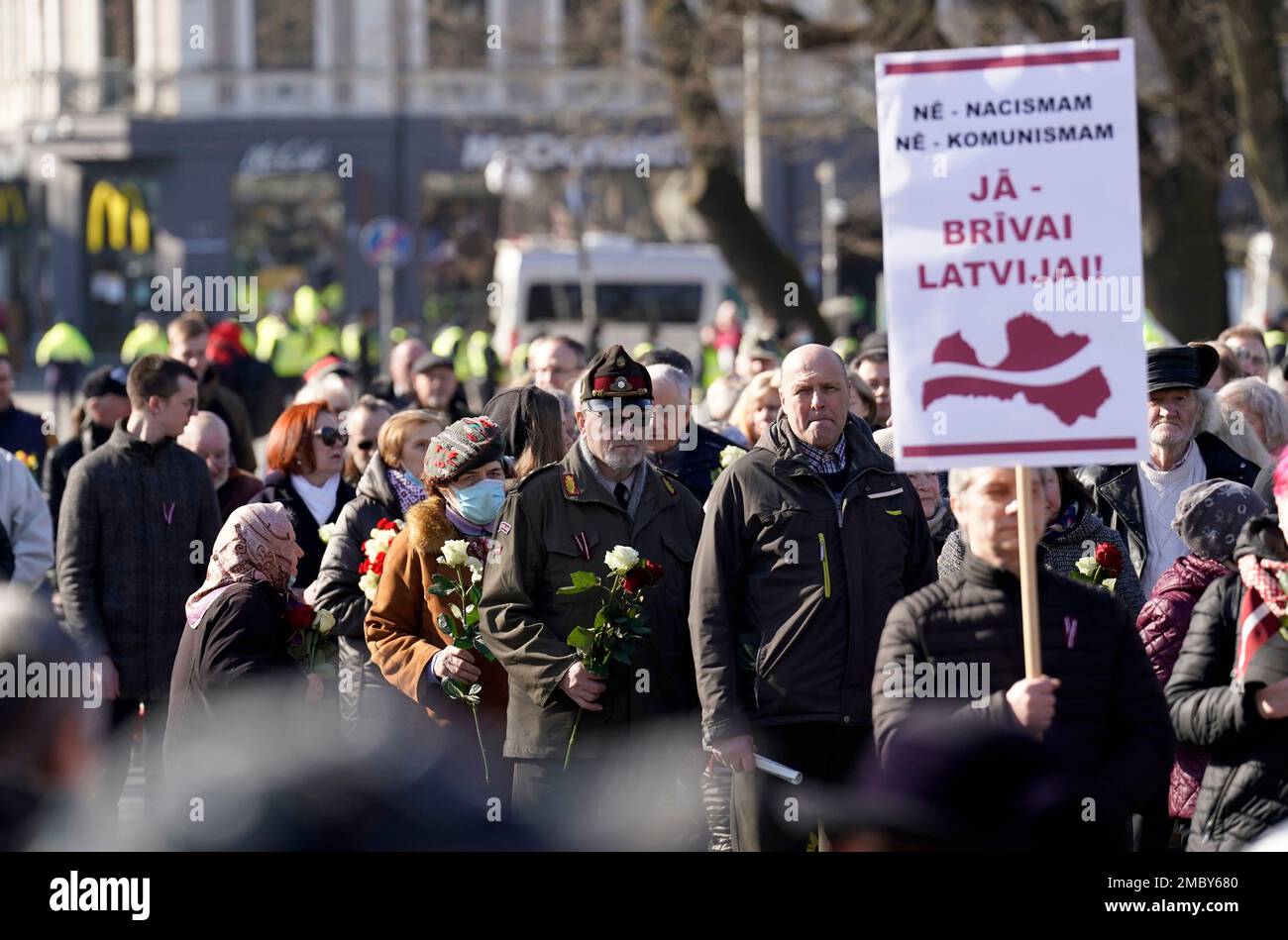 People carry flowers, one of them displaying a poster reading - "No ...