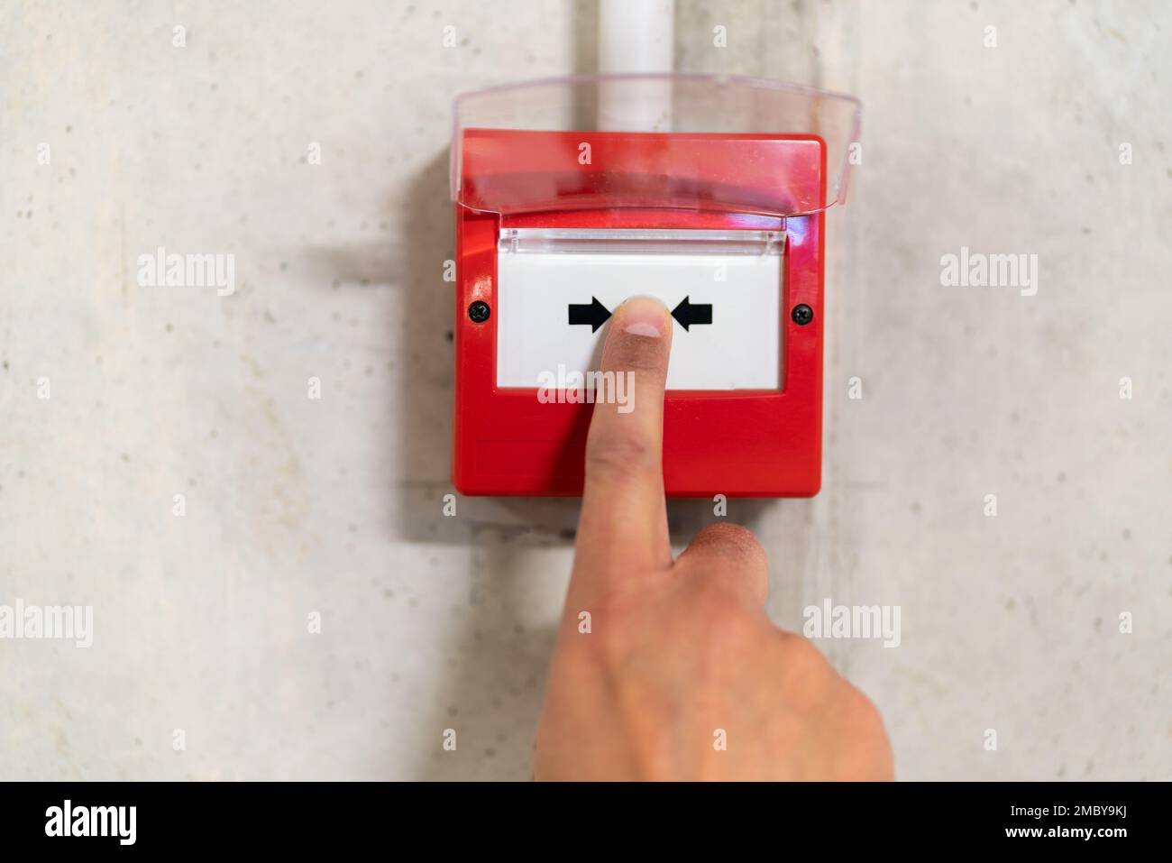 Close up of male hand pointing at red fire alarm switch on concrete ...