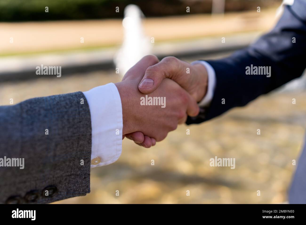 Anonymous businessmen in formal suits shaking hands while standing near ...