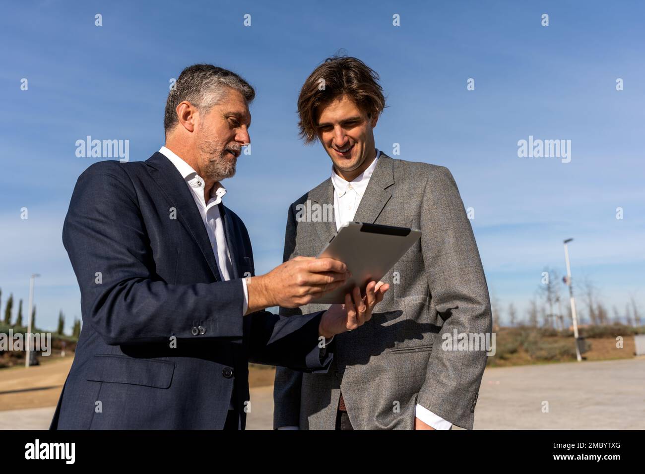 Low angle of positive businessmen in formal suits sharing tablet while ...