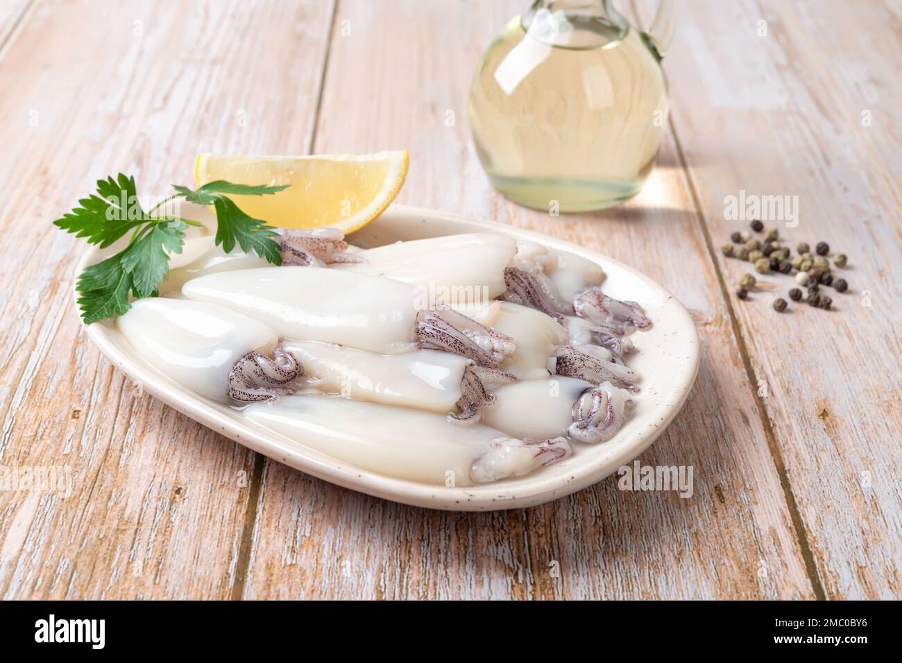 Fresh squid tubes on a plate over wooden table. Small calamary fillet ...