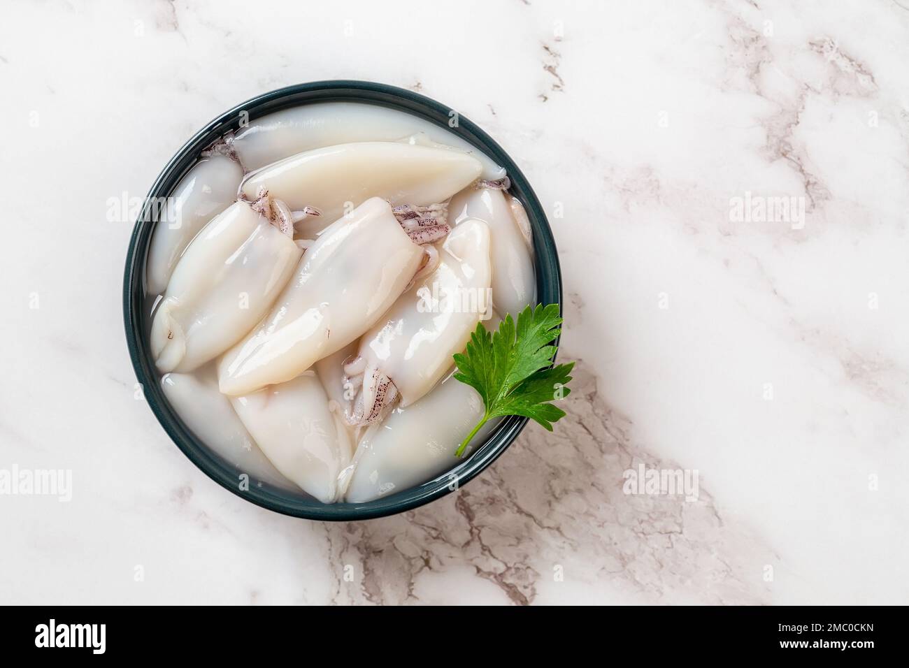 Raw squid fillet in a bowl over marble background. Small calamary tubes ...