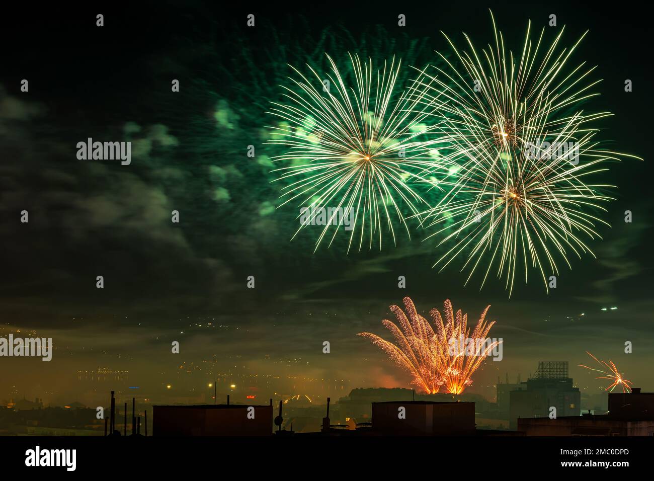 Colorful fireworks display over city at midnight. Green firework ...