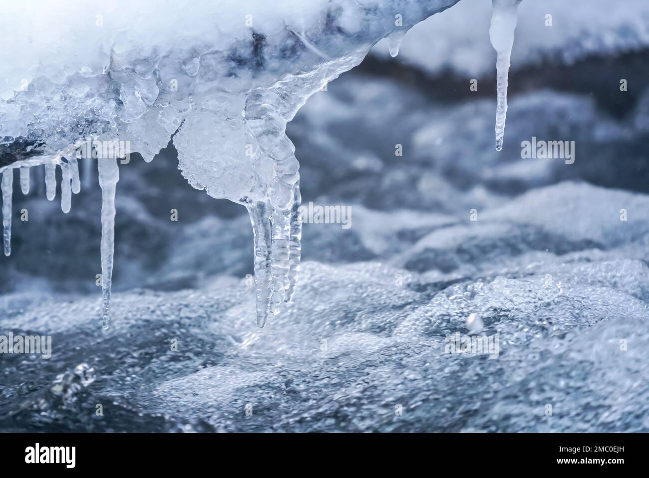 Ice on frozen river, closeup detail, water flows over rocks forming ...