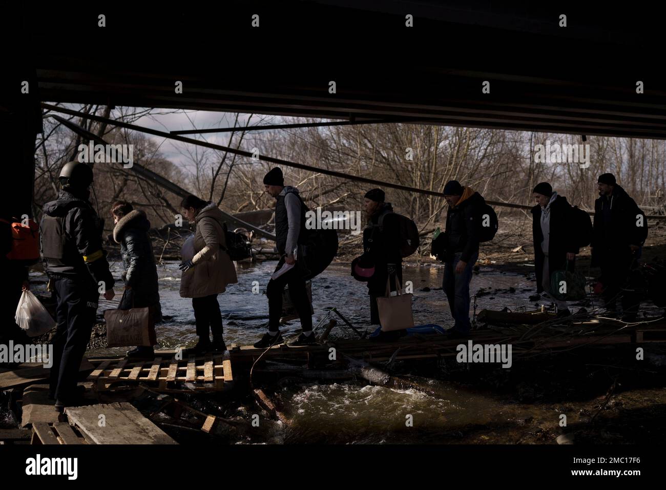 Ukrainians cross an improvised path under a destroyed bridge while ...