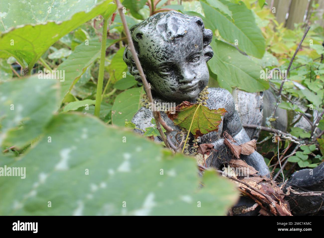 a small stone statue of a boy among green leaves Stock Photo - Alamy
