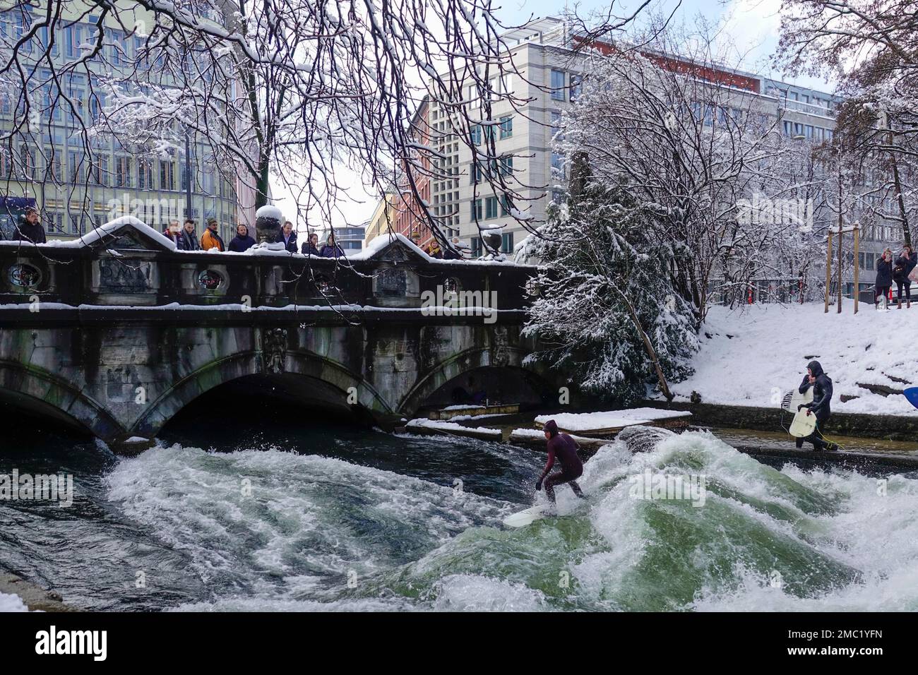 Surfers at the Eisbach wave below Prinzregentenstrasse, snow-covered in ...