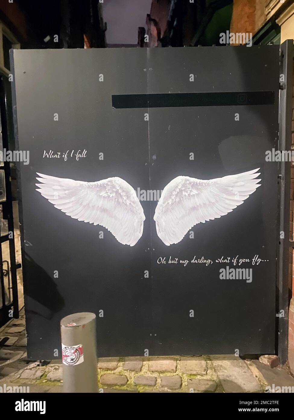 A vertical shot of a spray painting of white angel wings on a black ...
