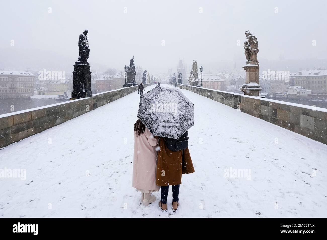 A couple crosses the medieval Charles Bridge as snow falls in Prague ...