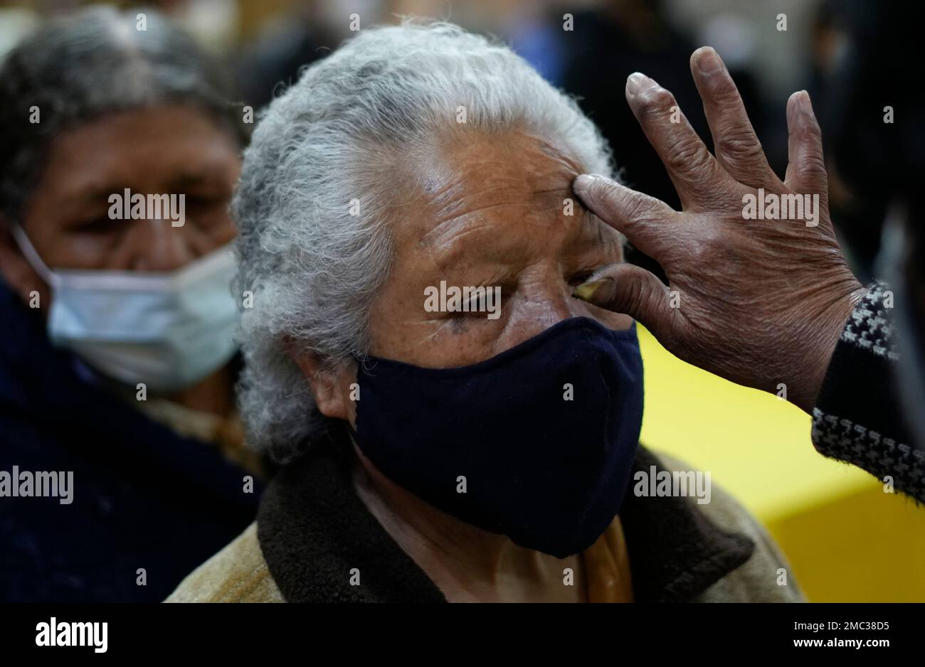 A priest's assistant marks the symbol of the cross on a woman's ...