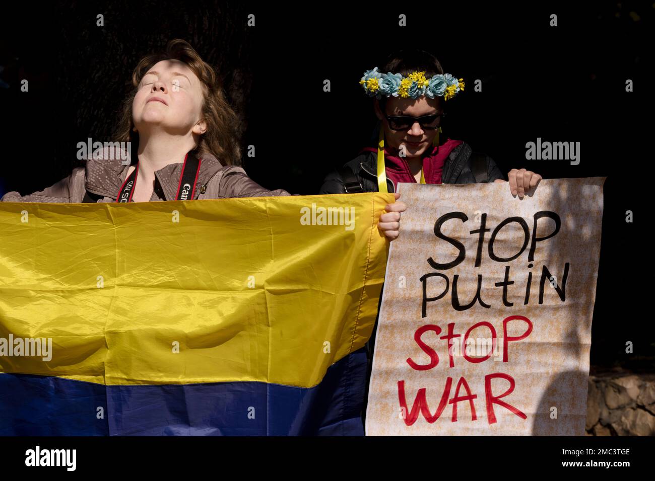 A woman holding the Ukrainian flag tilts her face towards the sun at a ...
