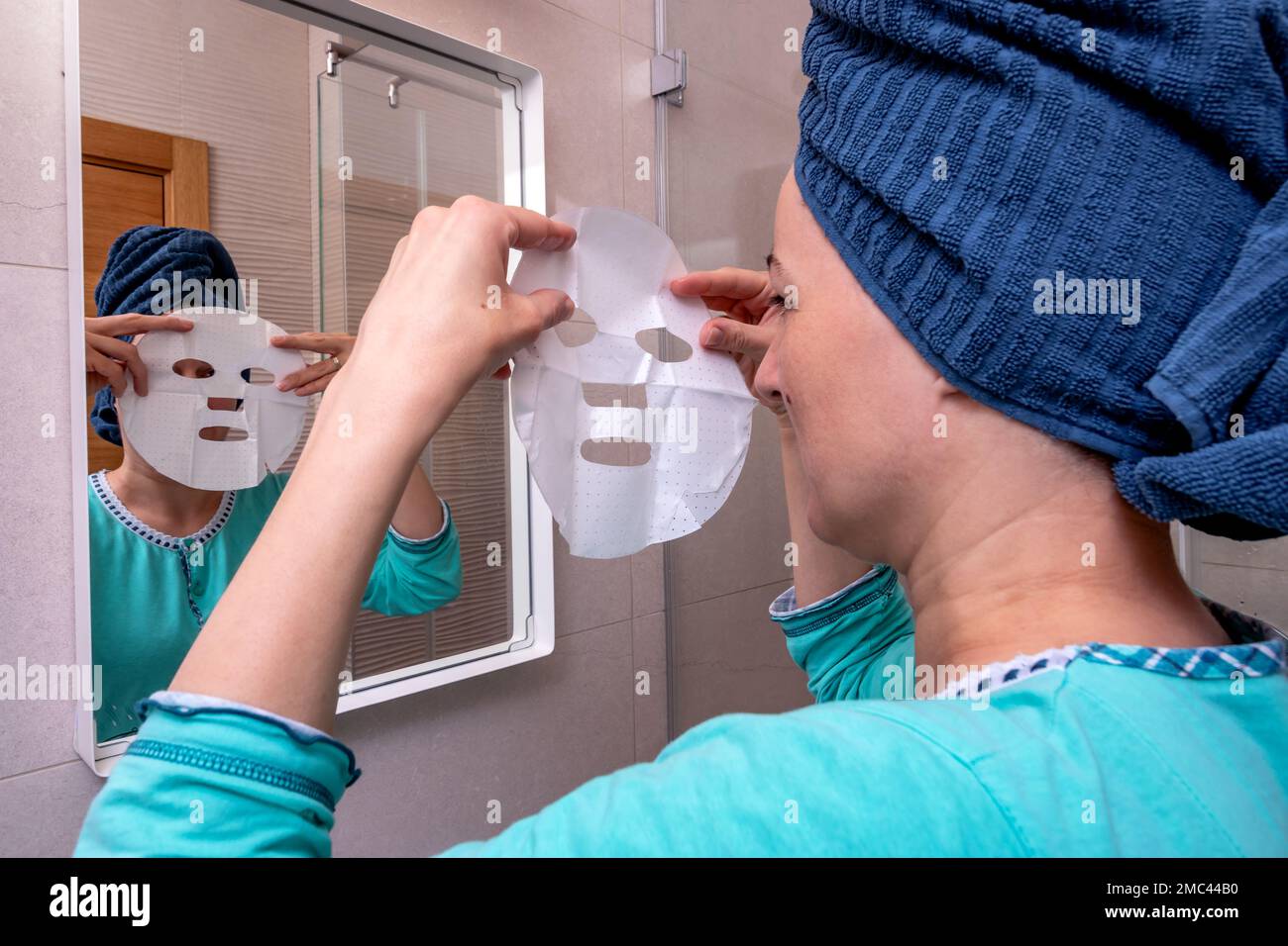 Portrait of a woman applying a cotton face mask in her bathroom after ...