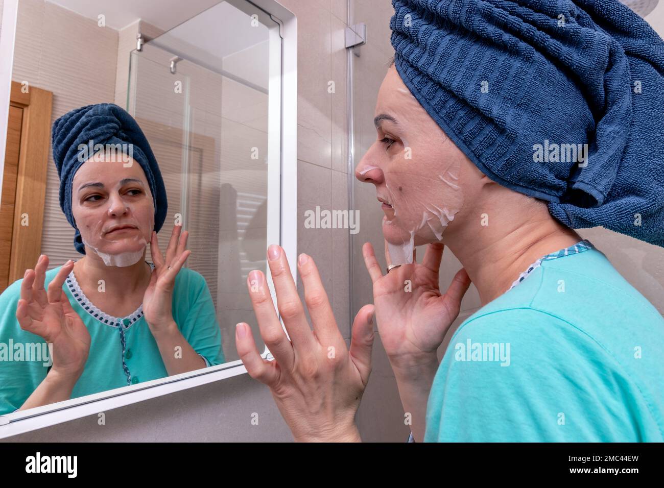 Portrait of a woman applying a cotton face mask in her bathroom after ...