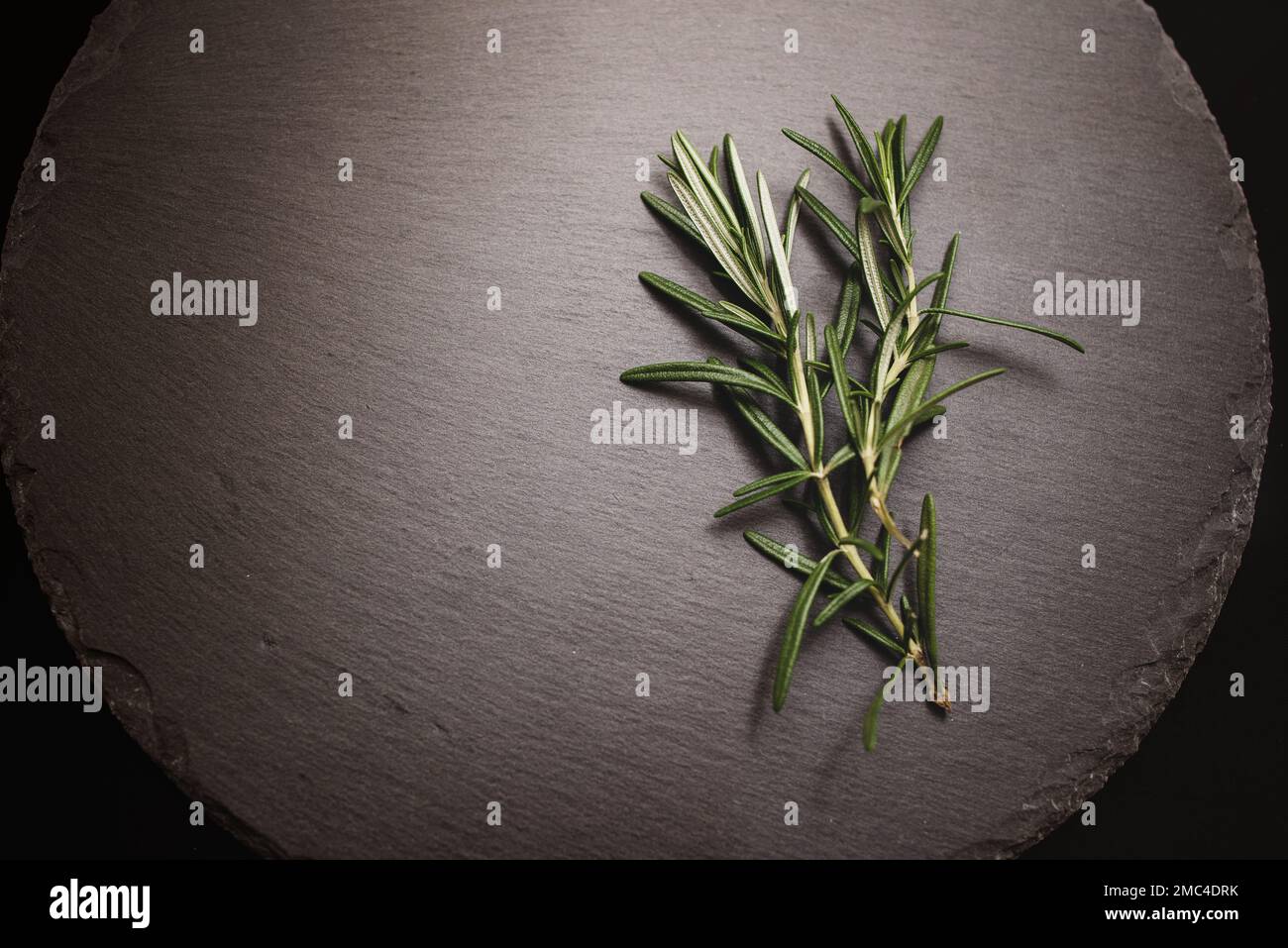 Rosemary herb on a gray stone board in a round shape on a black ...