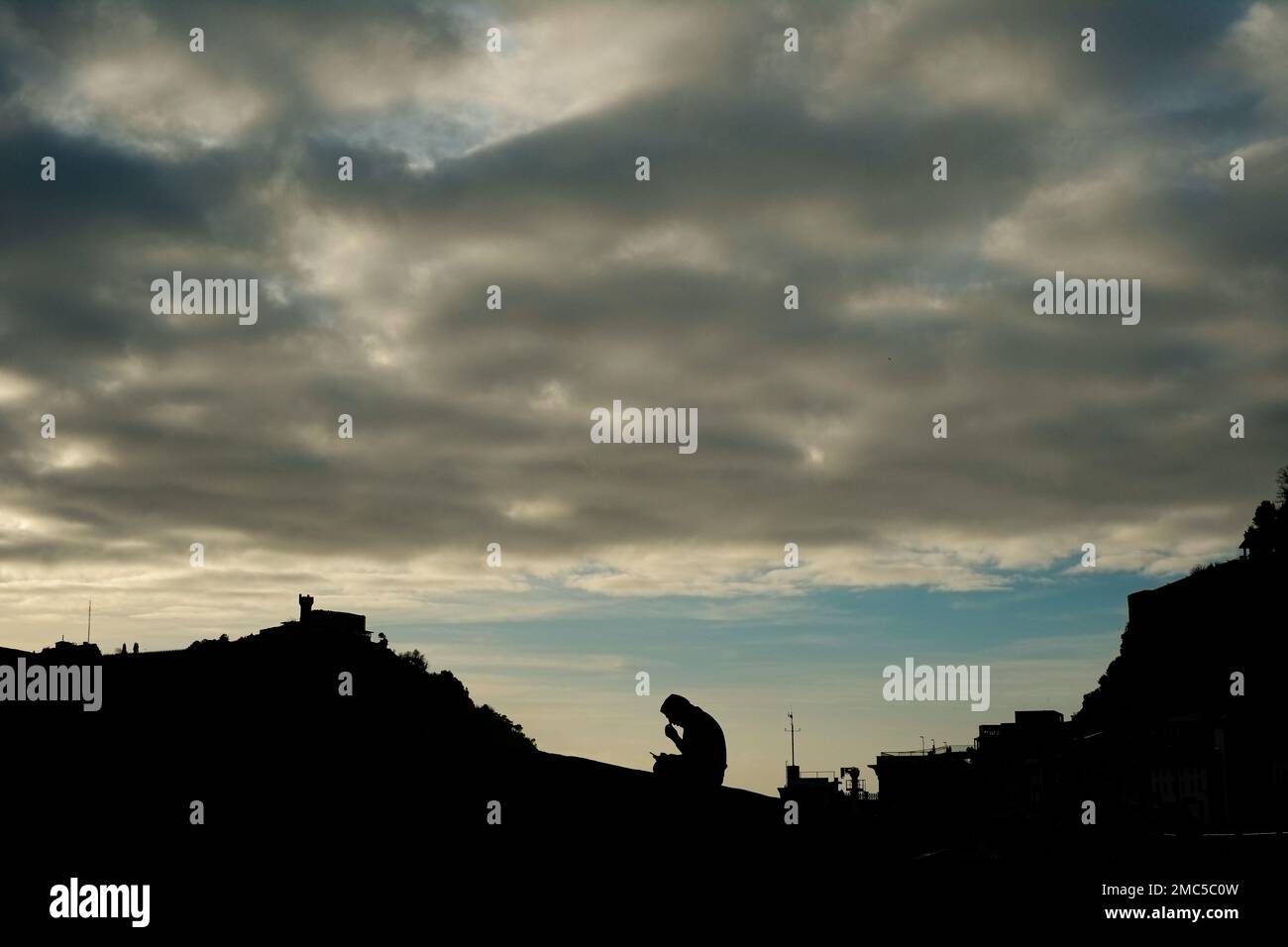 A person rests seating on a promenade as the sun sets on a winter day ...