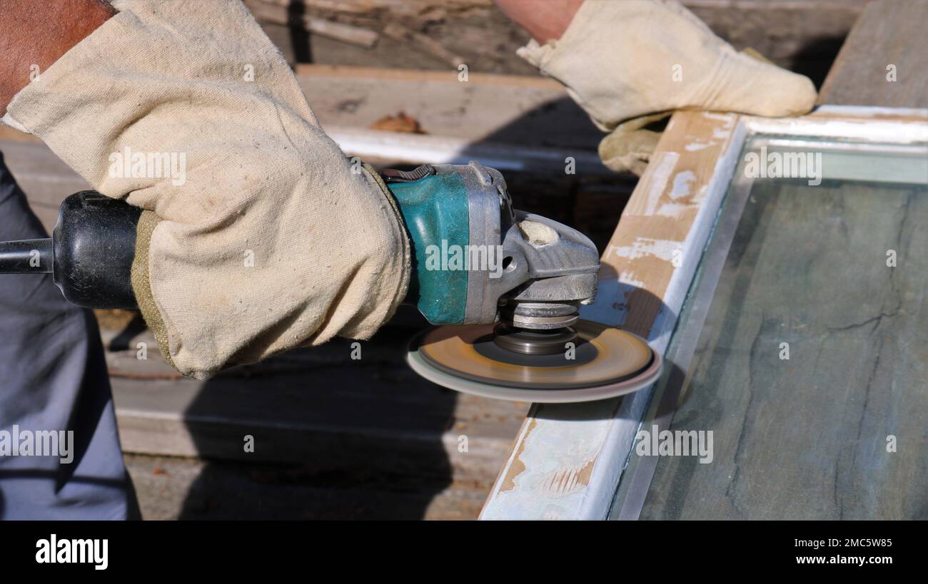 carpenter's hands in protective fabric mittens scraping off white paint ...