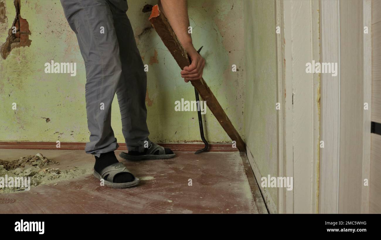 a man breaks a wooden floor plinth with an iron crowbar in a ...