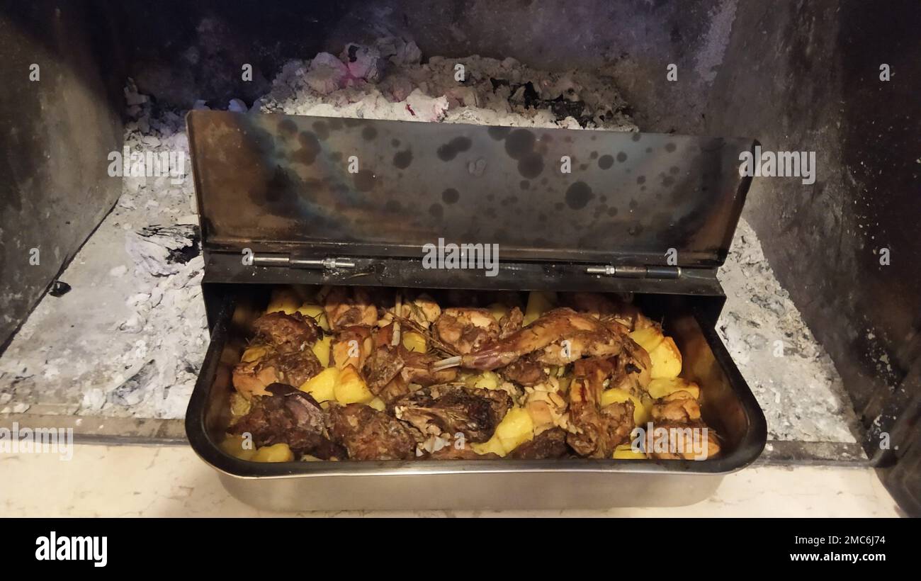 Image of a pan with meat and potatoes over hot coals in a fireplace ...