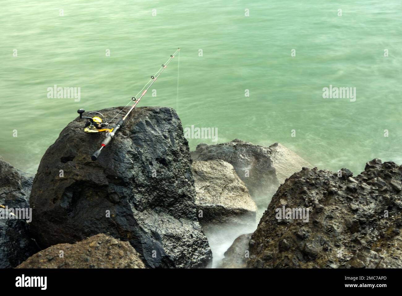 Fishing rod is left on the rock at the Marina Beach Semarang. Indonesia ...