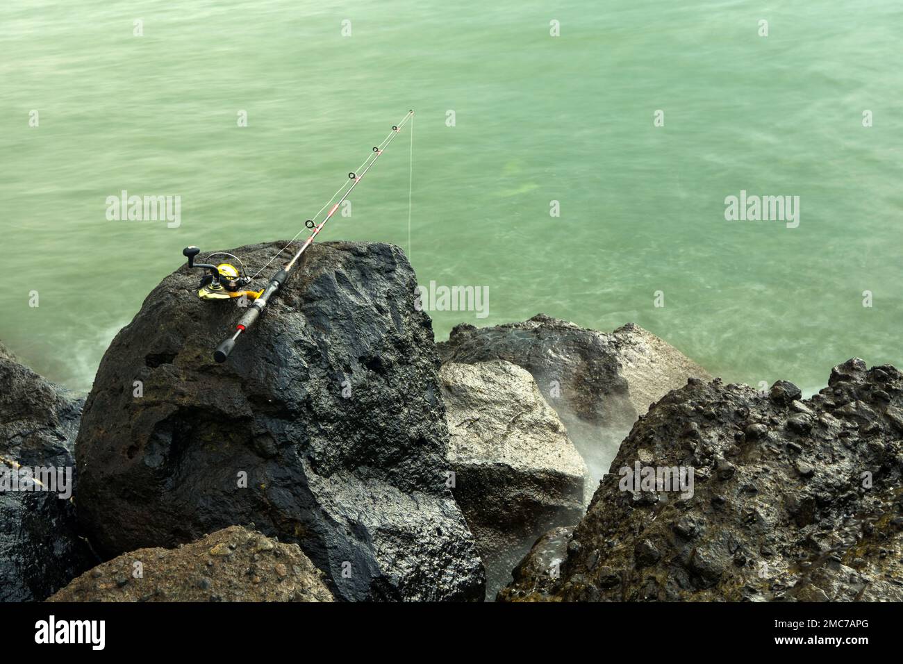 Fishing rod is left on the rock at the Marina Beach Semarang. Indonesia ...