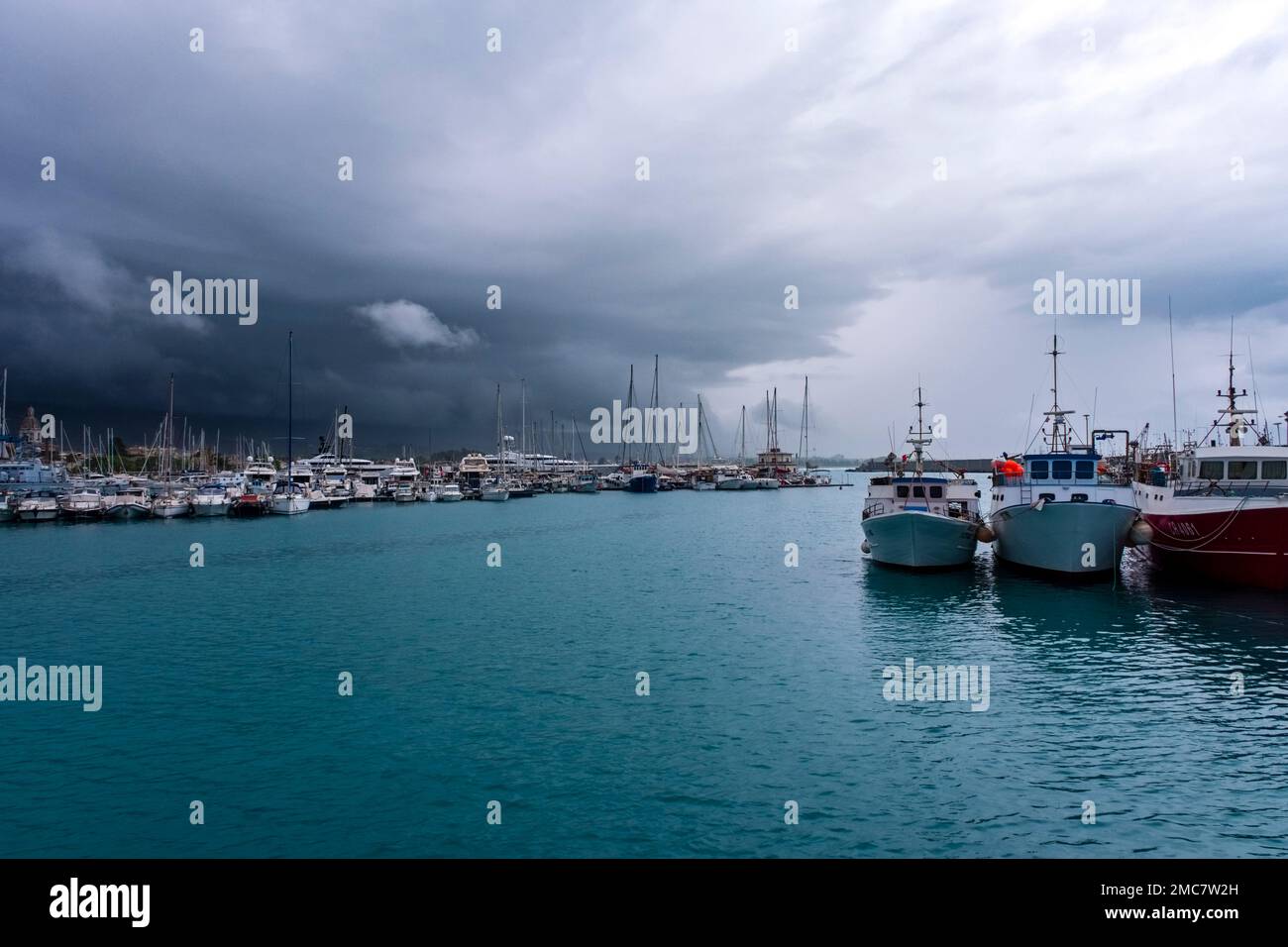 Dark storm clouds tower over the harbor of the town of Riposto, where ...