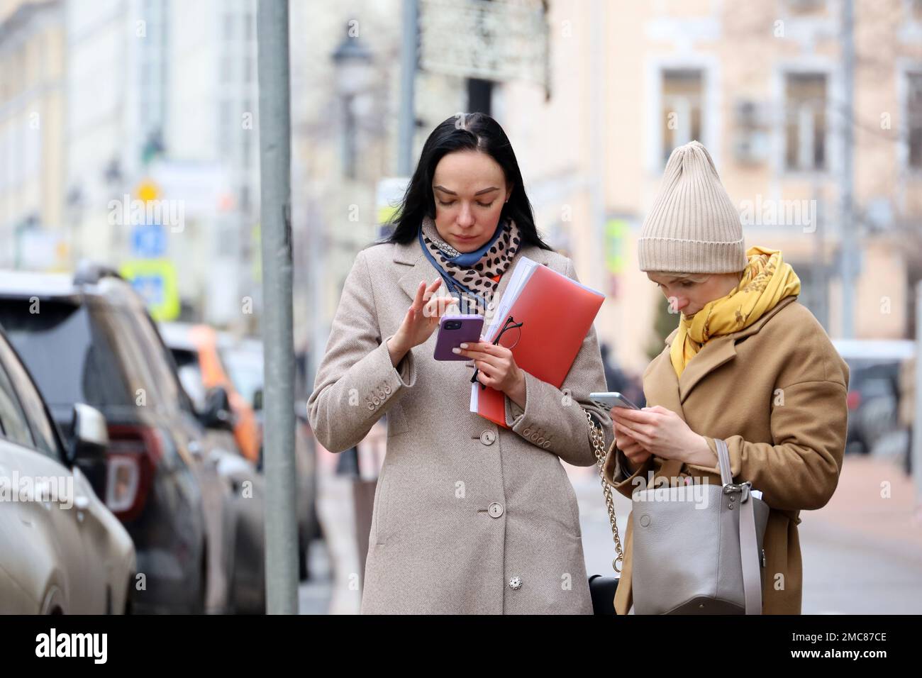 People using smartphones on city street. Two young women in warm ...