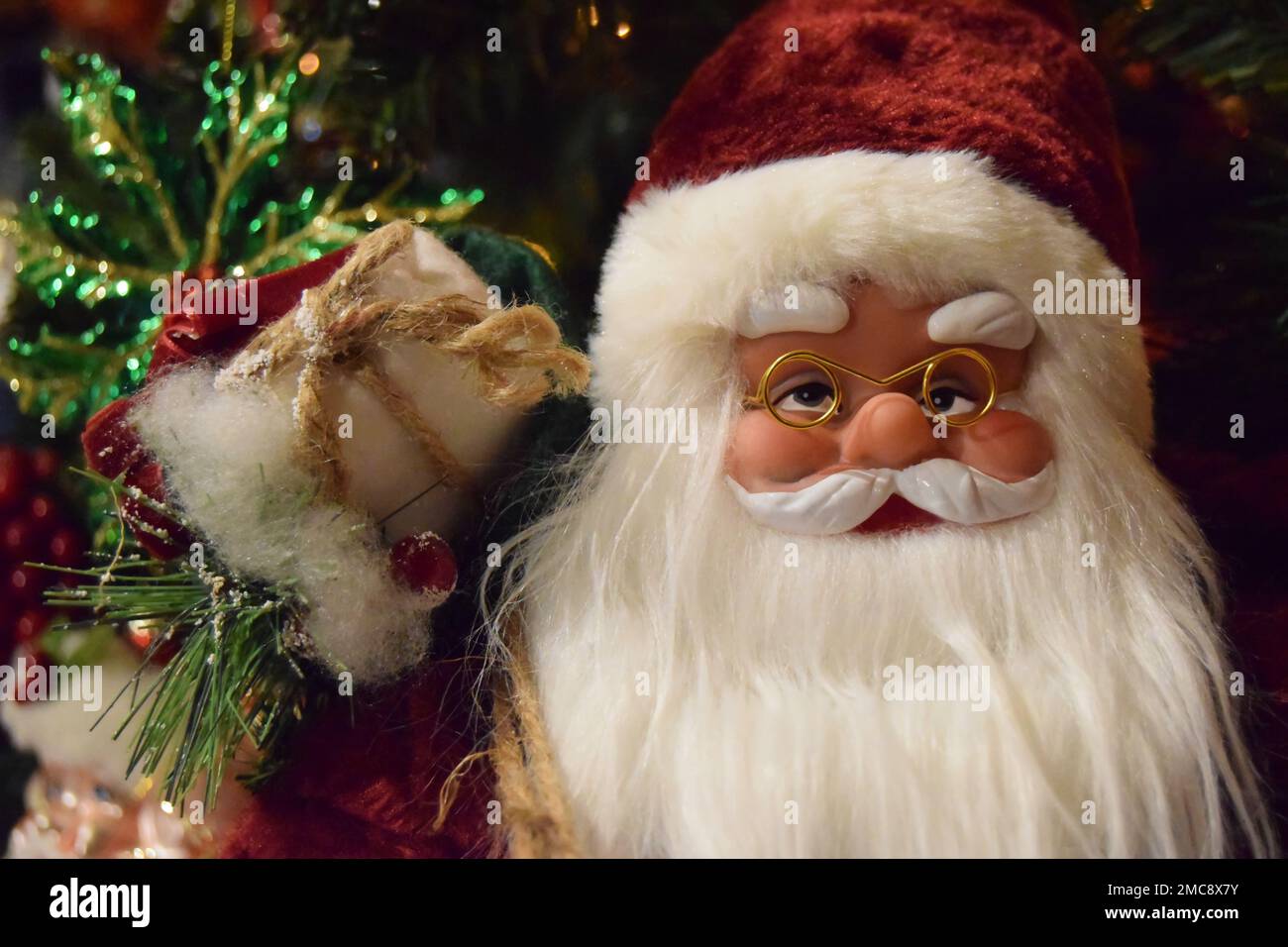 A festive Santa Claus dressed in a traditional red & white hat carrying ...