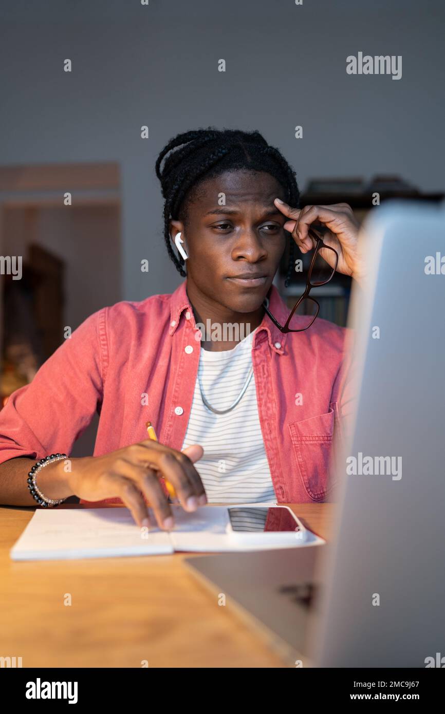 Tired black young man touch forehead thinking looking at laptop screen ...