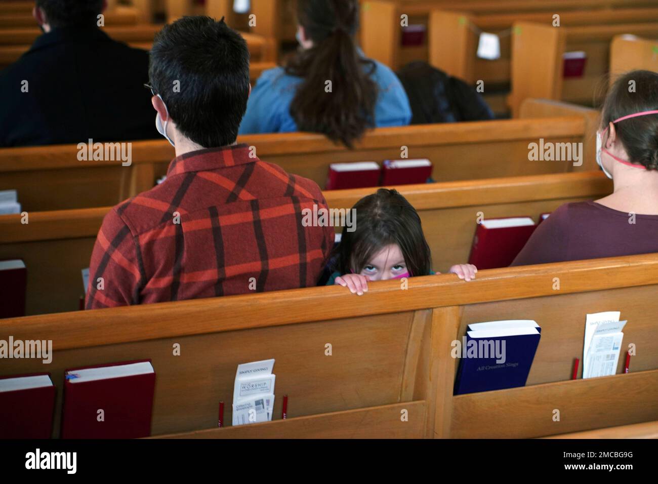 A young girl peeks above the pew next to her parents during the service ...