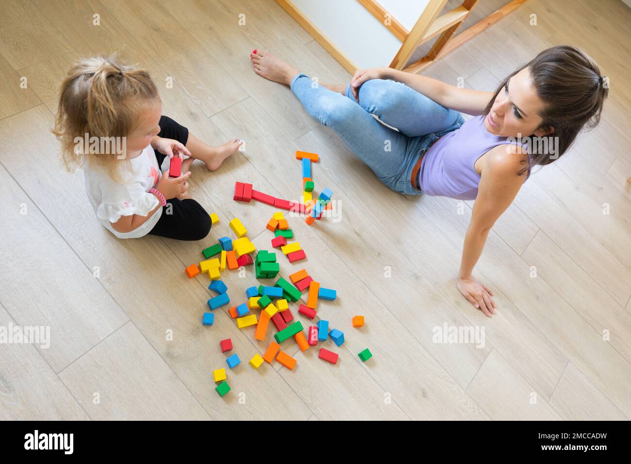 In a bright, light-colored room, mother and daughter play with colorful ...