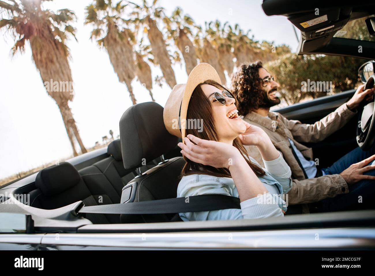 Happy young adult couple enjoying summer vacation driving a cabriolet ...