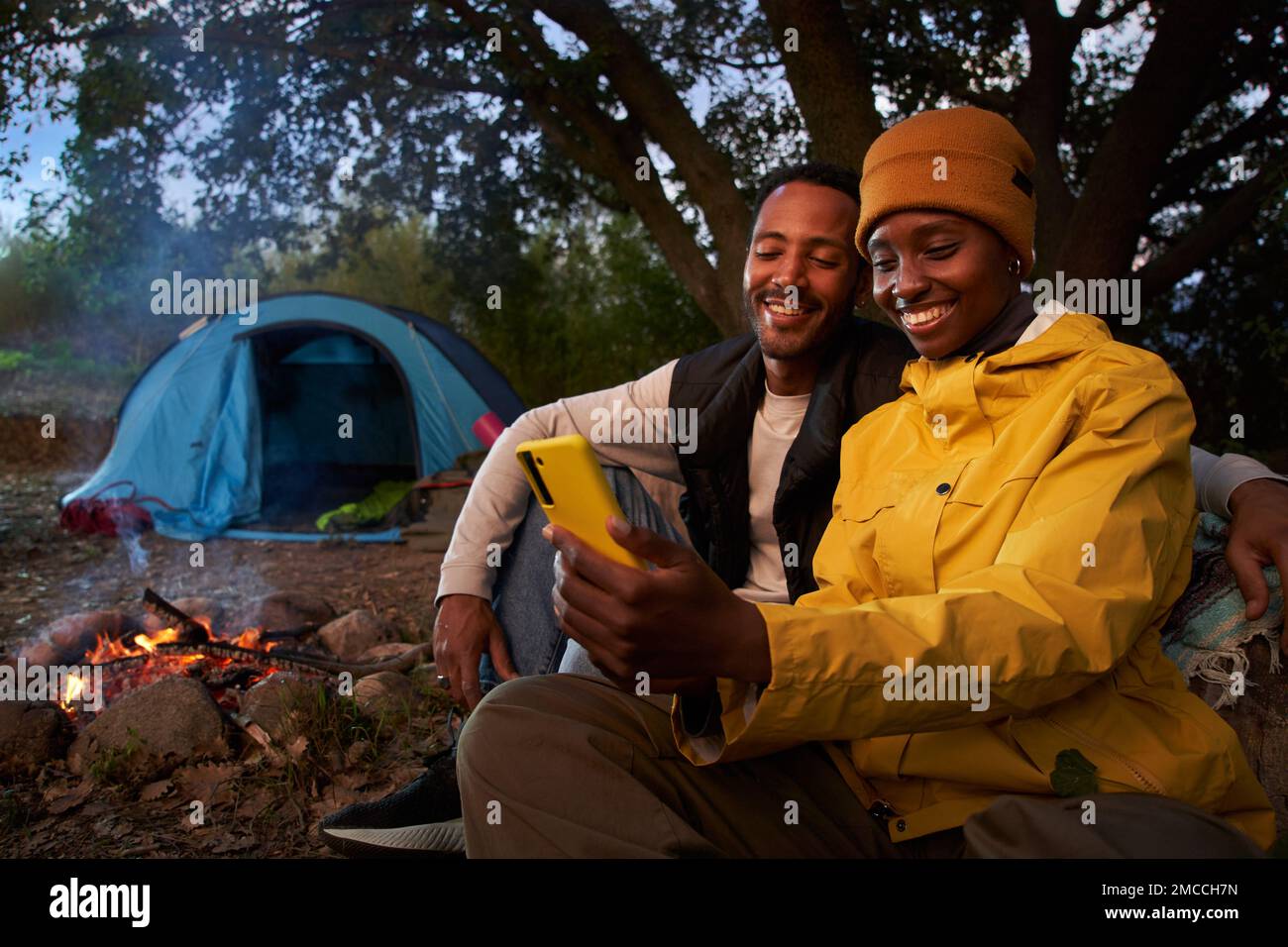 African couple using cellphones and sitting during camping together on ...