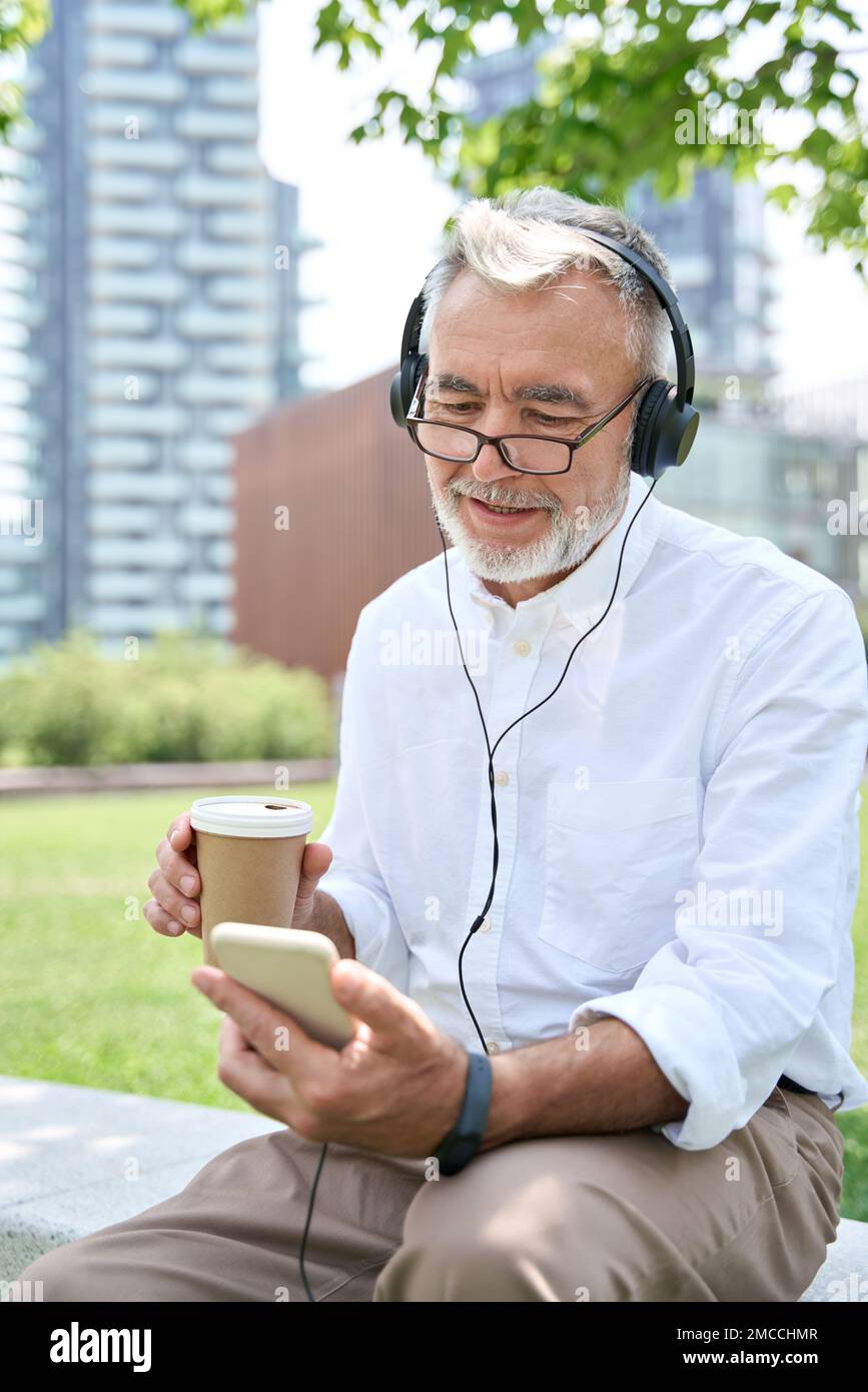 Older business man using smartphone wearing headphones having hybrid ...